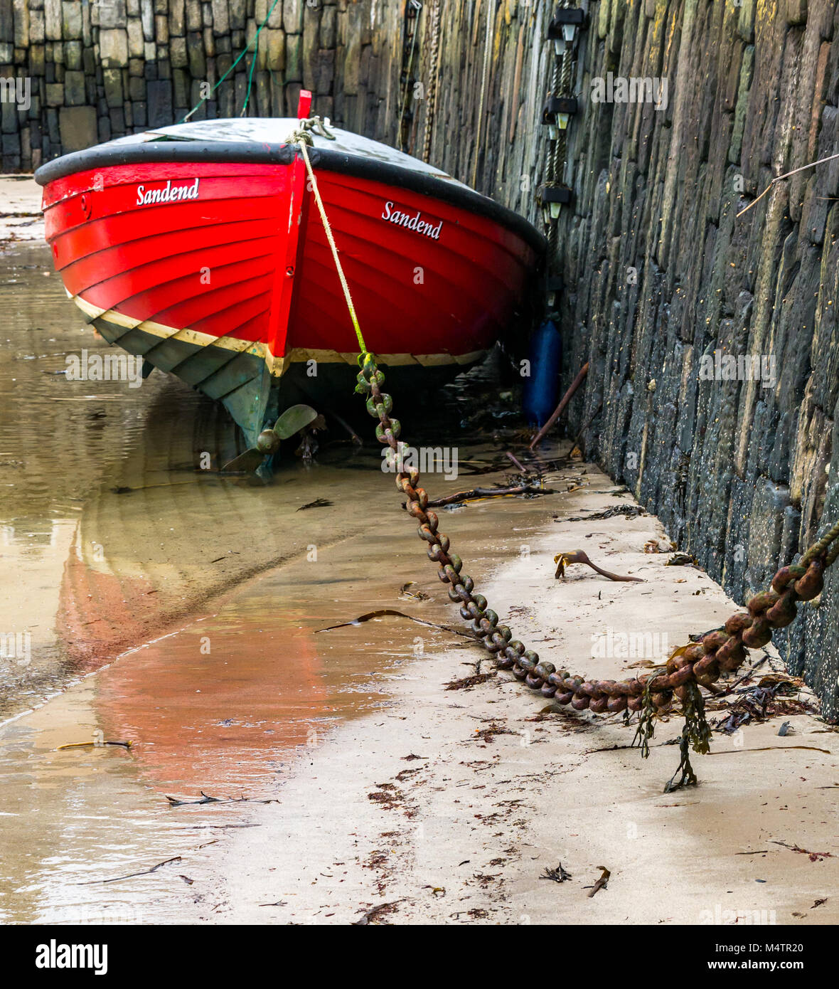Close up of chained small red rowing boat at low tide from Sandend ...