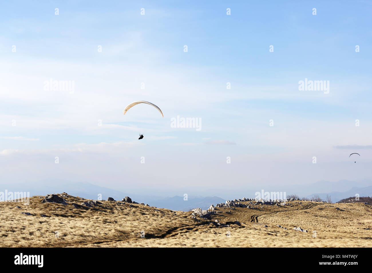 Sky diver floating in the air over grass covered mountain landscape ...