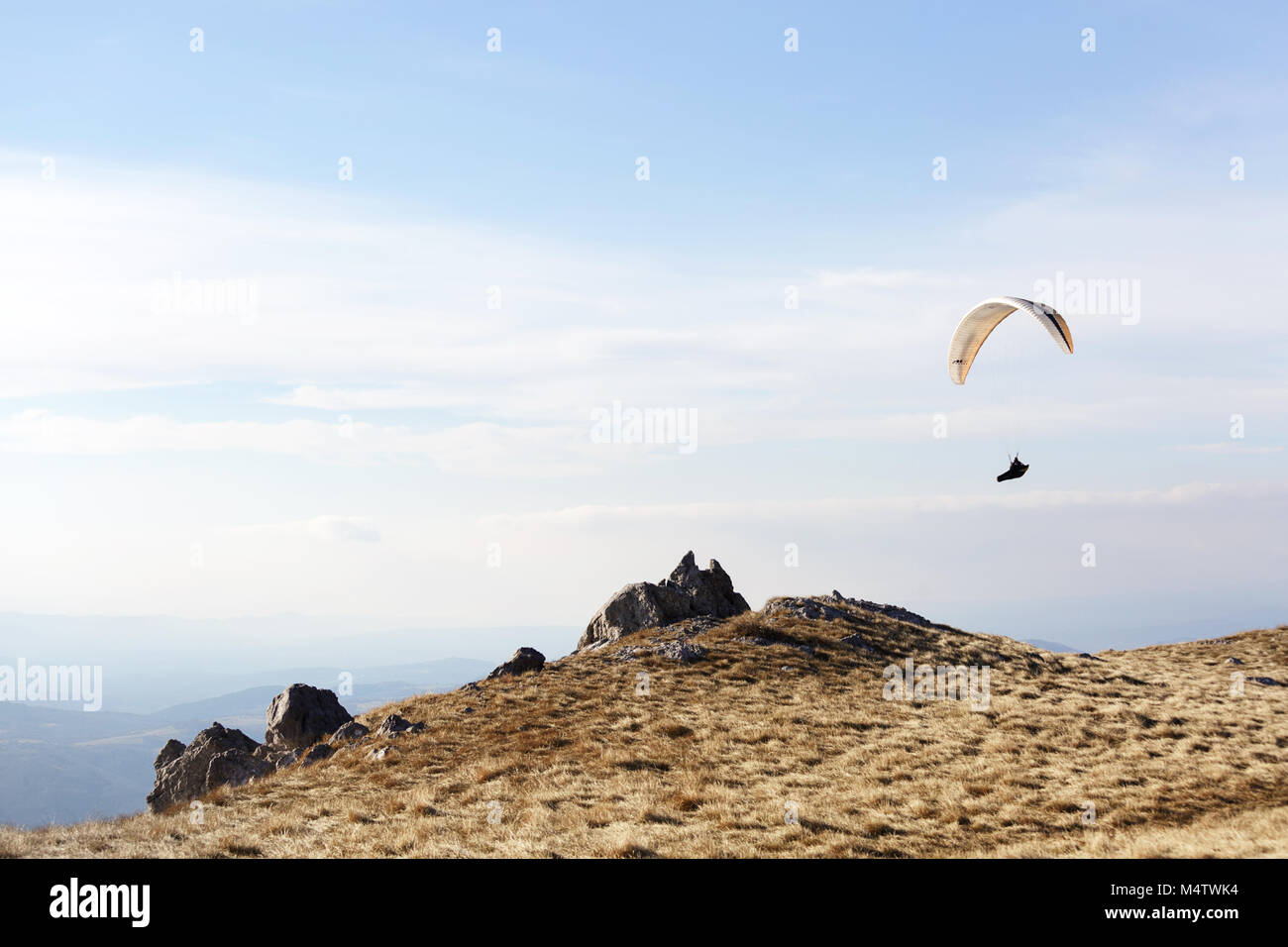 Sky diver floating in the air over grass covered mountain landscape ...