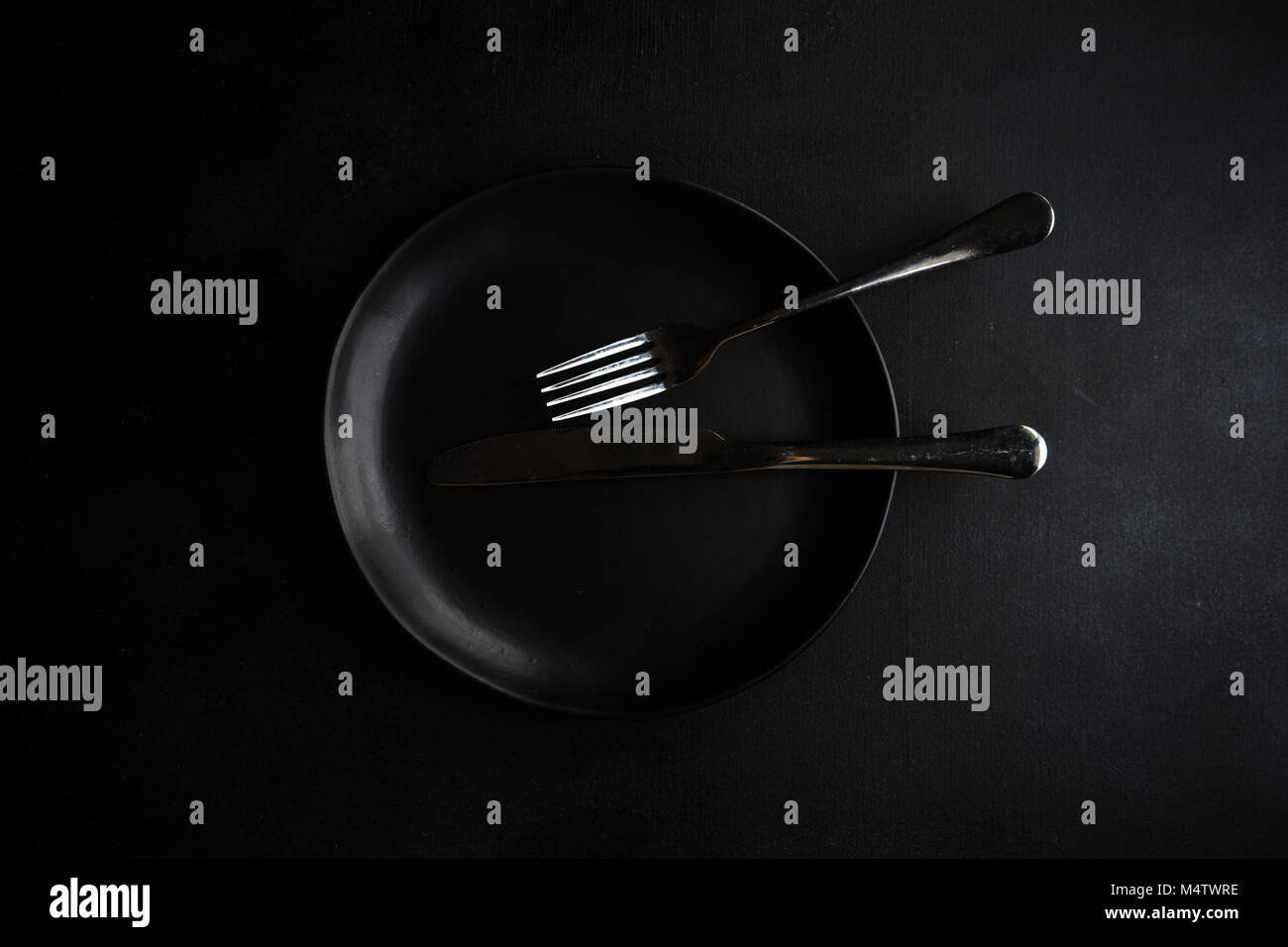 Dark table setting with black plate with silverware Stock Photo - Alamy