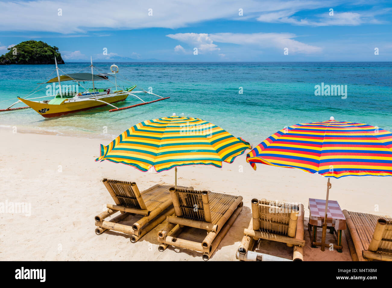 Bumboo sun lounges with sun umbrellas on the sand, local fishing boat ...