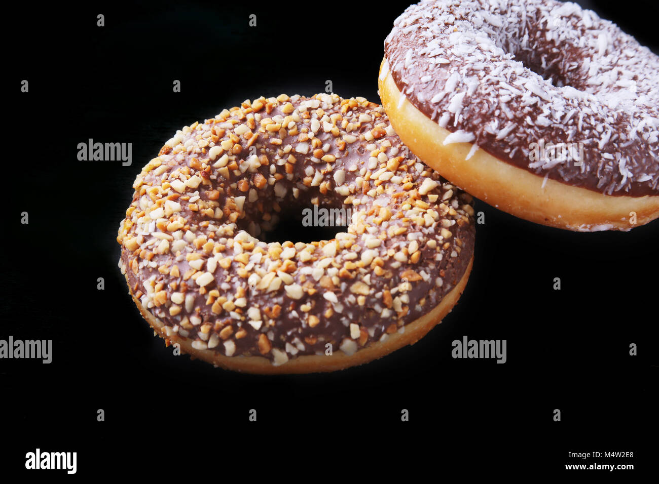 Assorted doughnuts in the glaze, colorful sprinkles and nuts on a black ...