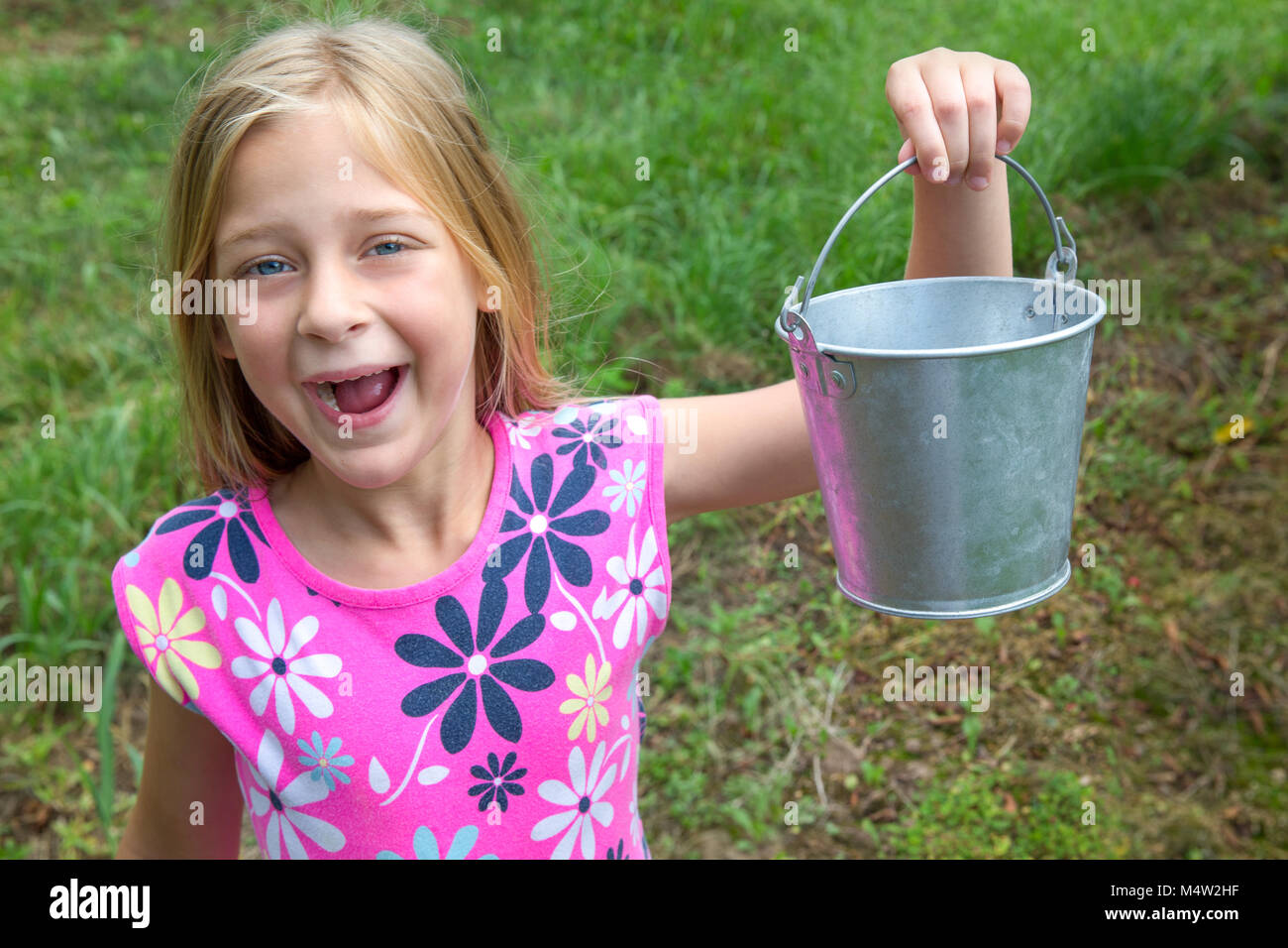 Smiling girl holding an empty tin pail or bucket. Grinning and looking ...