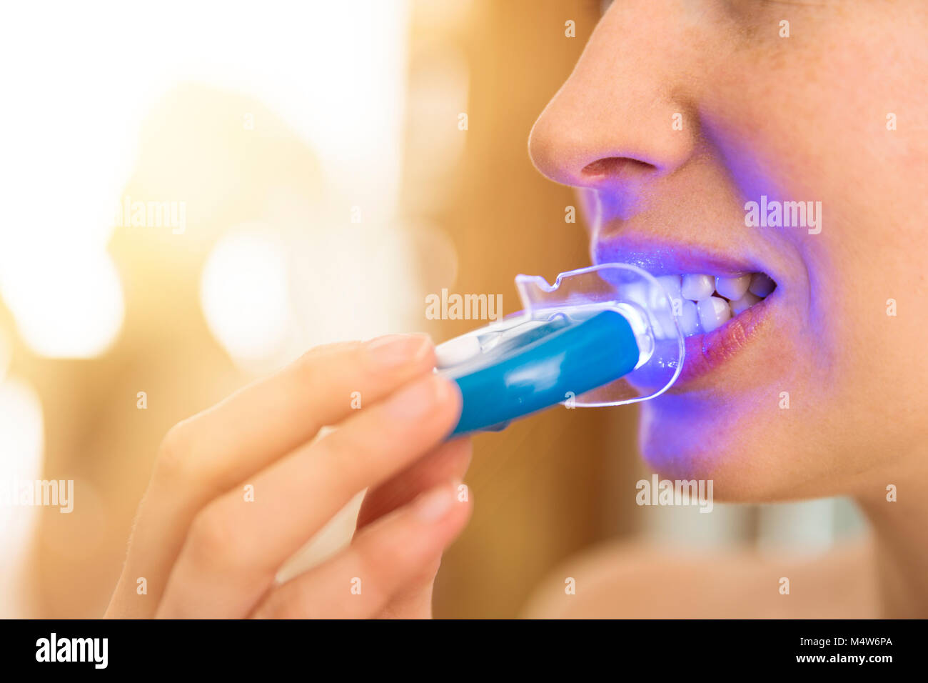 Woman is whitening teeth with special toothpaste and LED light at home ...
