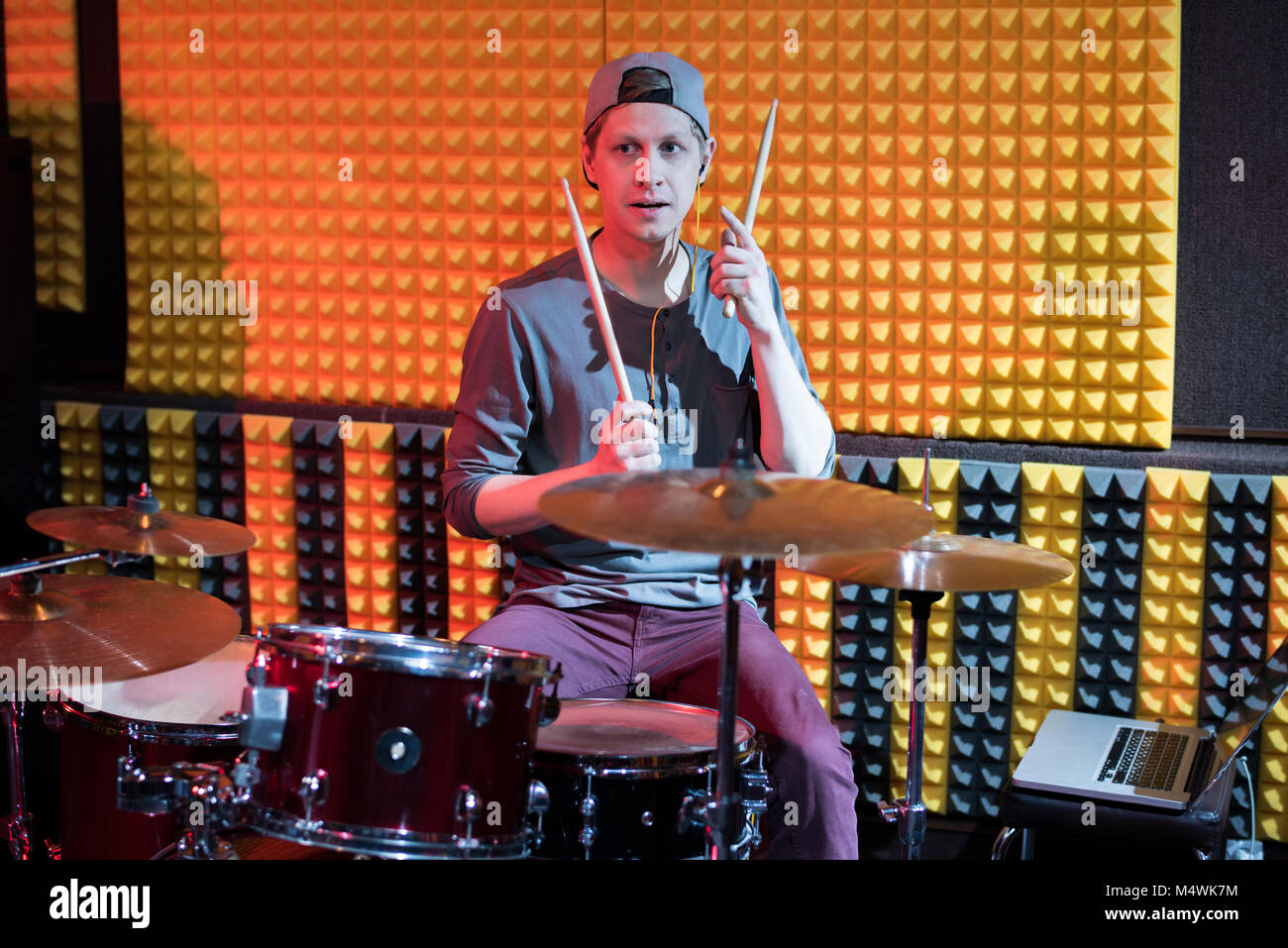 Portrait of young man playing drums performing in dim recording studio ...