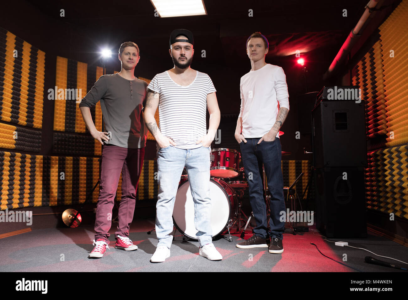 Full length portrait of modern music band posing in recording studio ...