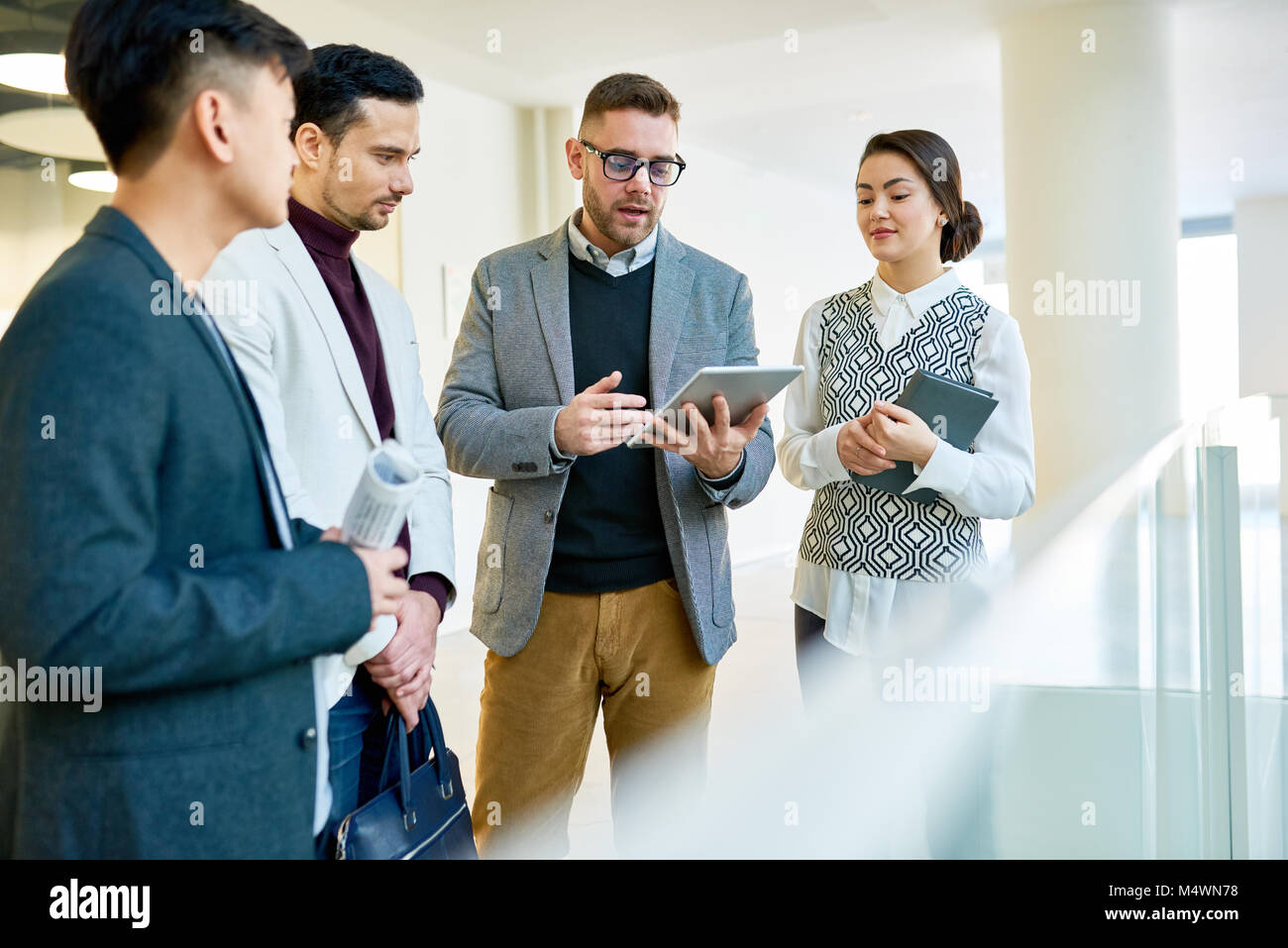 Group of four young business people discussing work while standing in ...
