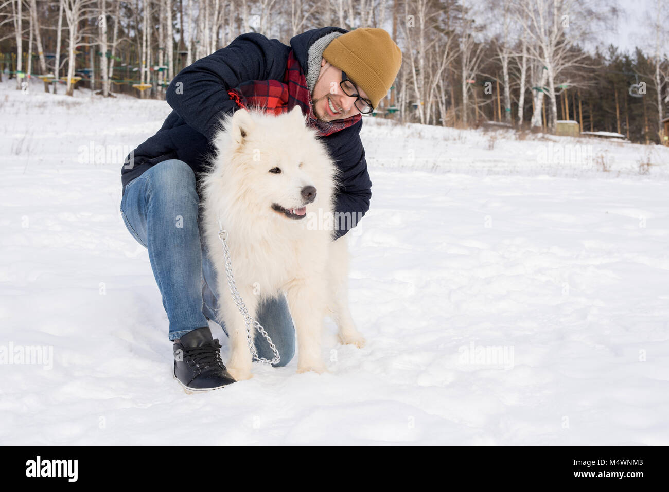 Full length portrait of modern adult man petting white Samoyed dog ...
