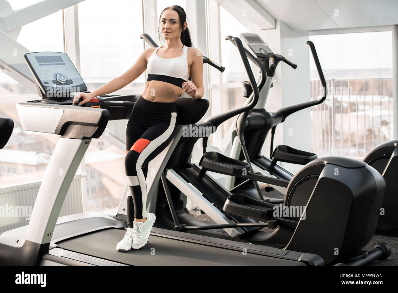 Full length portrait of fit young woman posing standing on treadmill in ...