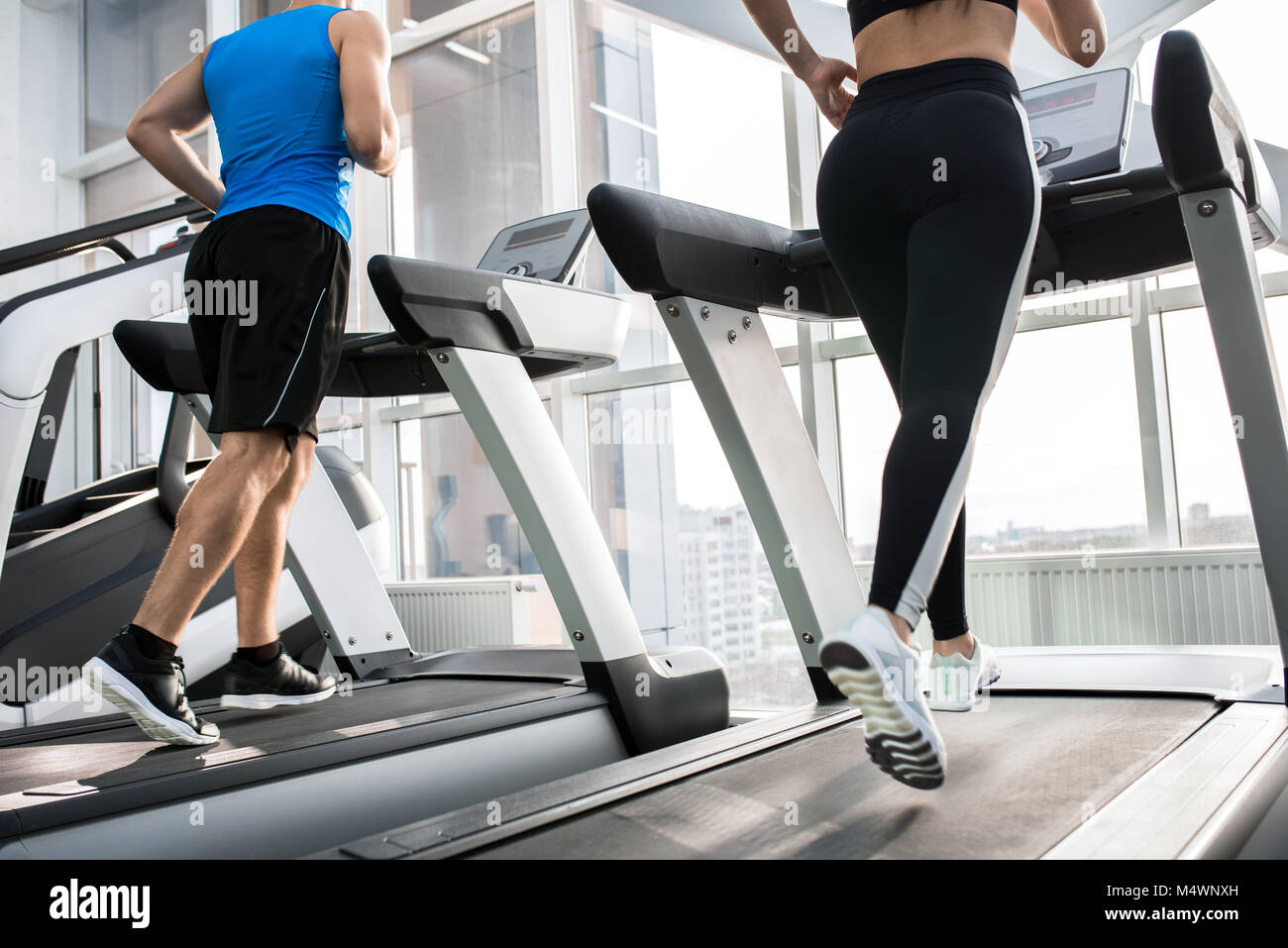 Mid-section back view of two fit young people, man and woman, running ...