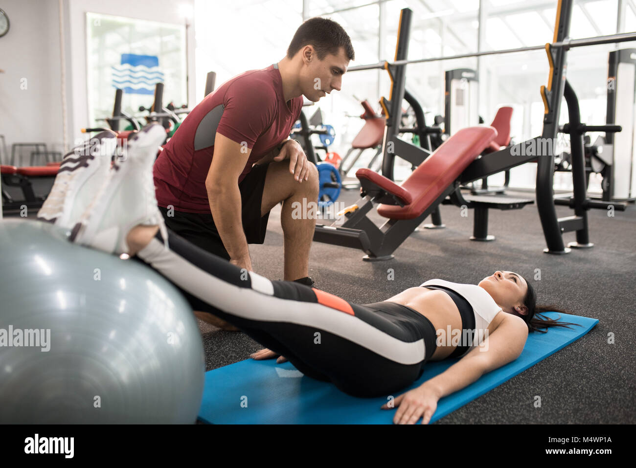 Full length portrait of muscular fitness coach helping young woman ...