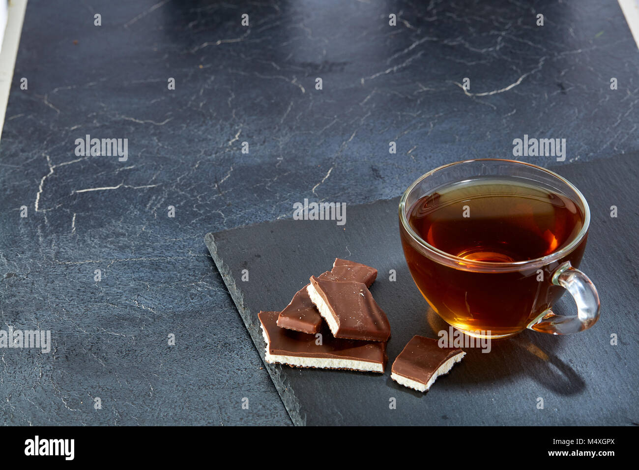 A transparent glass cup of black tea with chocolate pieces on a dark ...