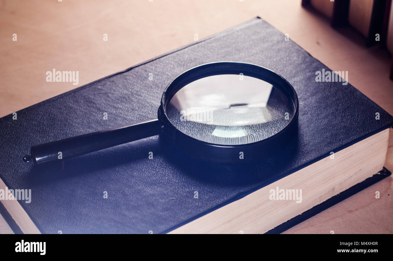Magnifier with black handle is on the cover of the book, glare and ...