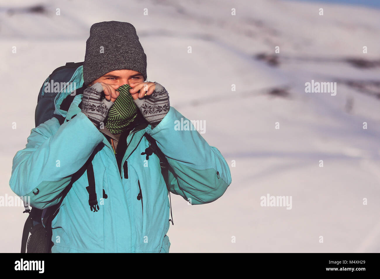 Man, covering his face with a scarf, wearing grey hat and blue anorak ...