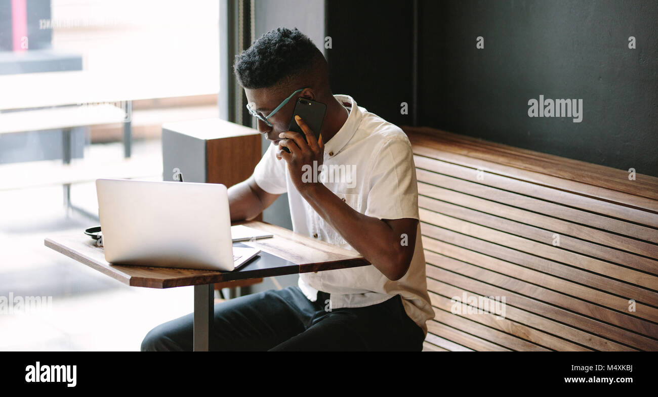 Man writing notes while talking over mobile phone with a laptop ...