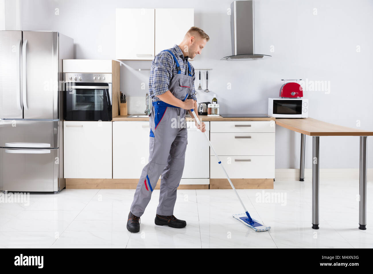 Happy Young Male Worker Mopping Floor With Mop In Kitchen Stock Photo ...