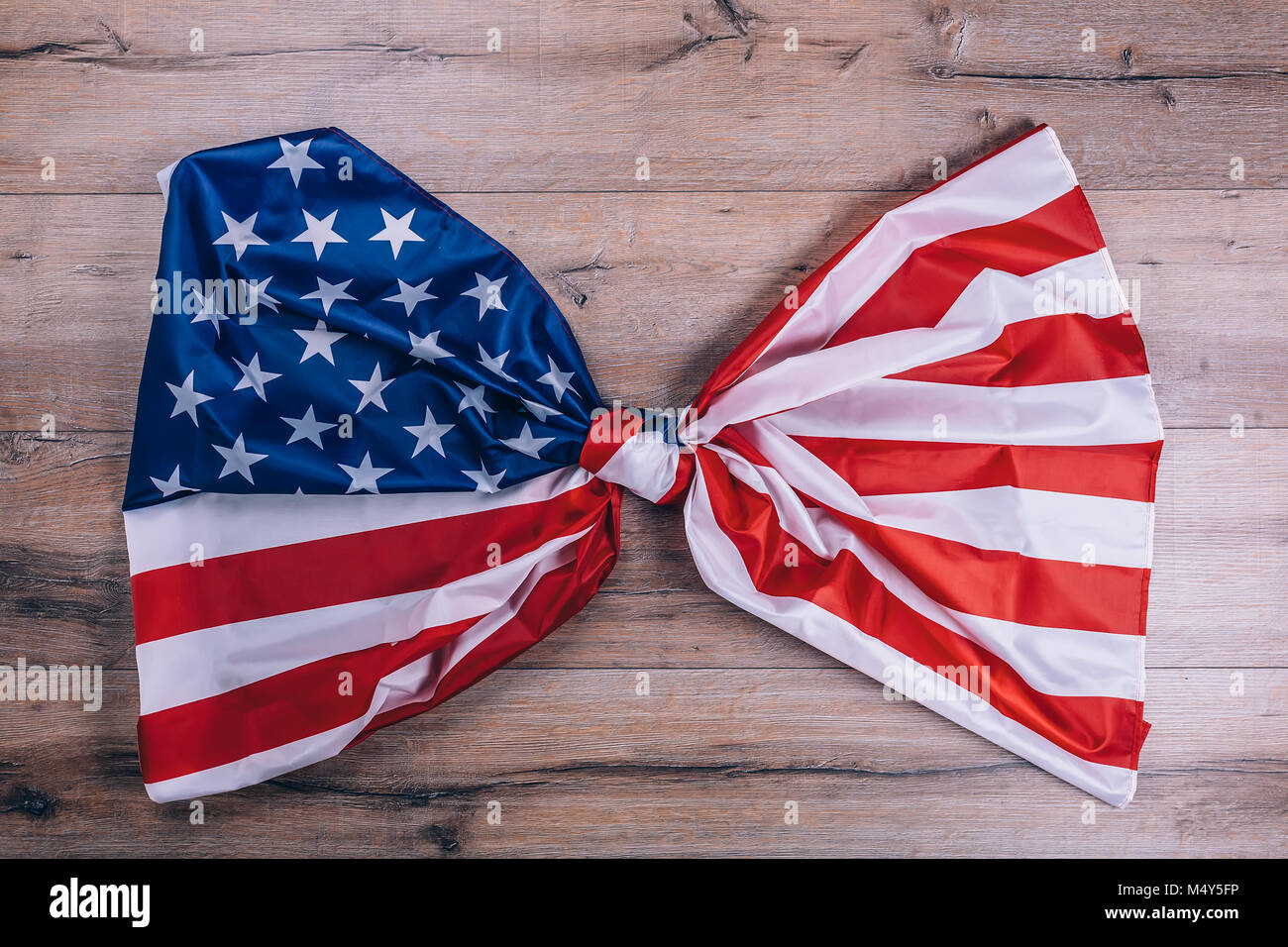 American flag, tied in a knot, on dark wooden wall. Visual concept of ...