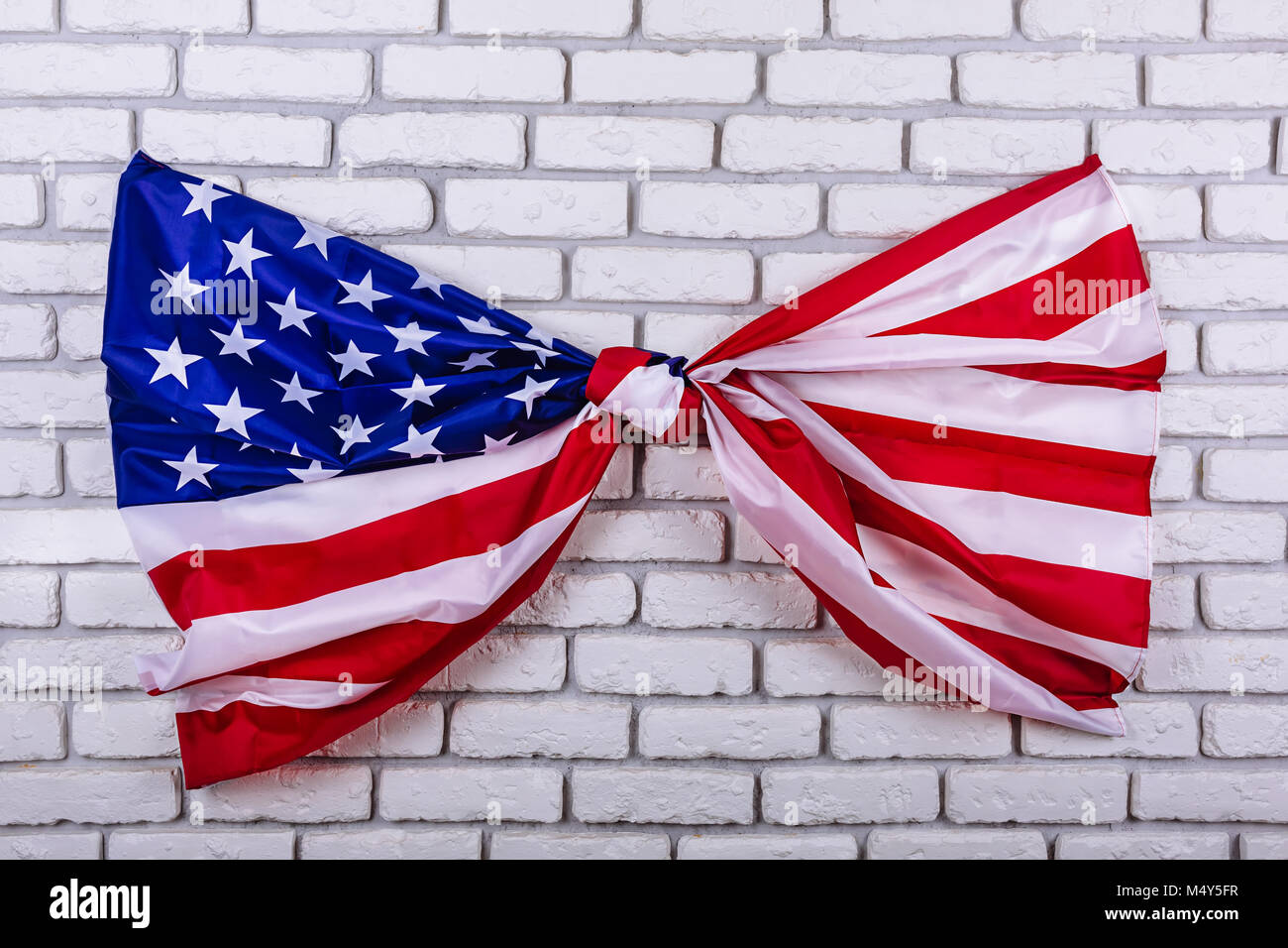 American flag, tied in a knot, on a white brick wall. Visual concept of ...