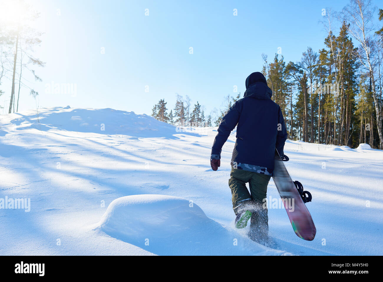 Back view of young snowboarder running up snowy hill to go freestyle ...