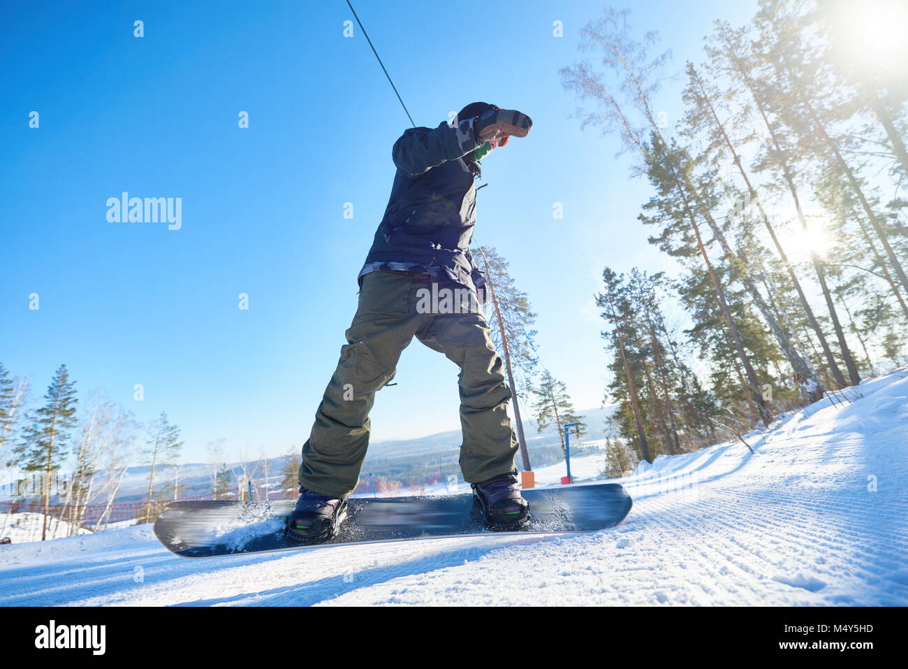 Low angle portrait of young man riding snowboard on mountain piste at ...
