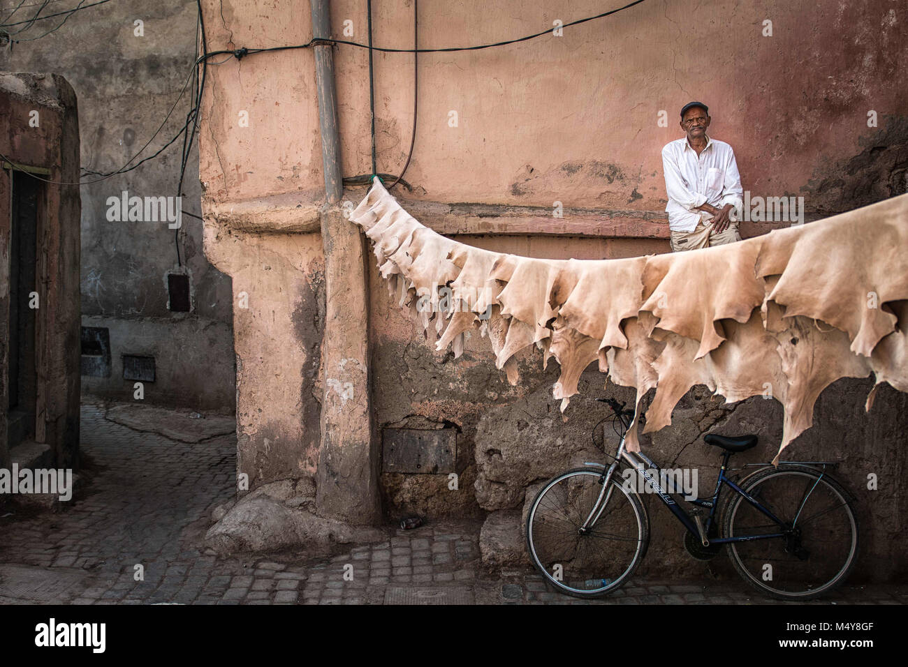A local tannery worker leans on a wall on some stairs. Leather skins ...