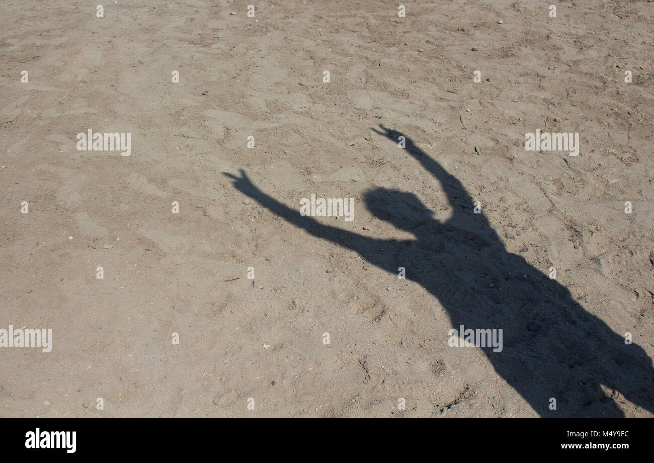 Shadow of man doing peace/victory sign with two hands on sand ...