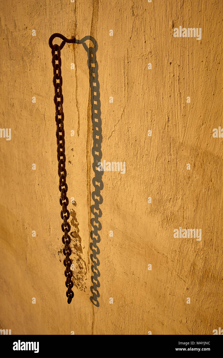 Old iron chain hanging from a peg in a stucco brick wall Stock Photo ...