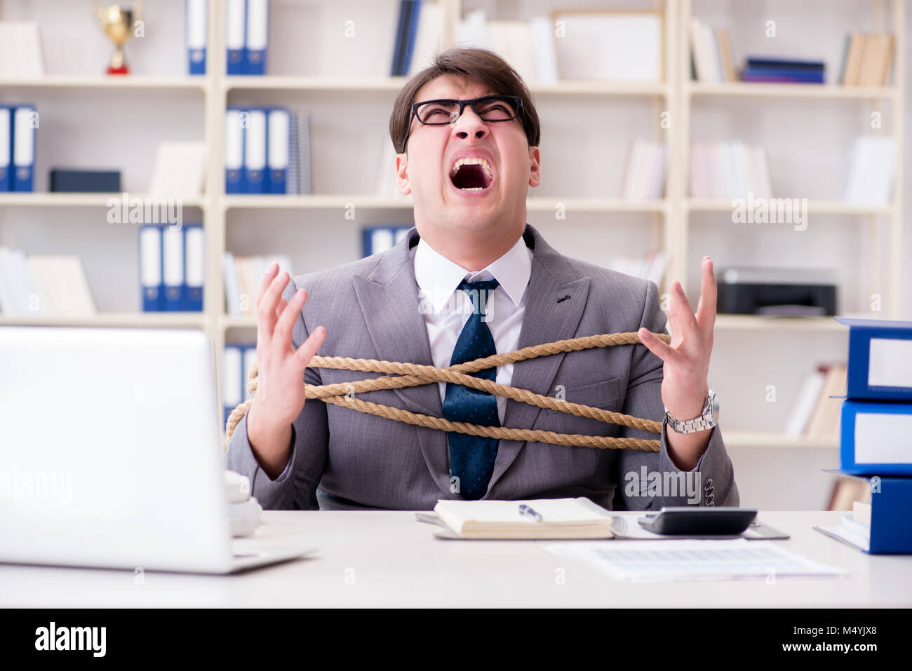Businessman tied up with rope in office Stock Photo - Alamy