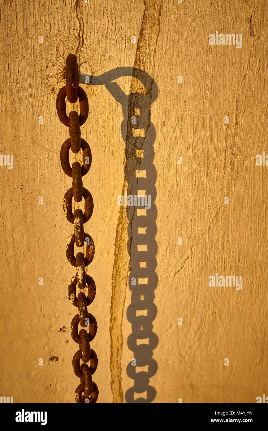 Old iron chain hanging from a peg in a stucco brick wall Stock Photo ...