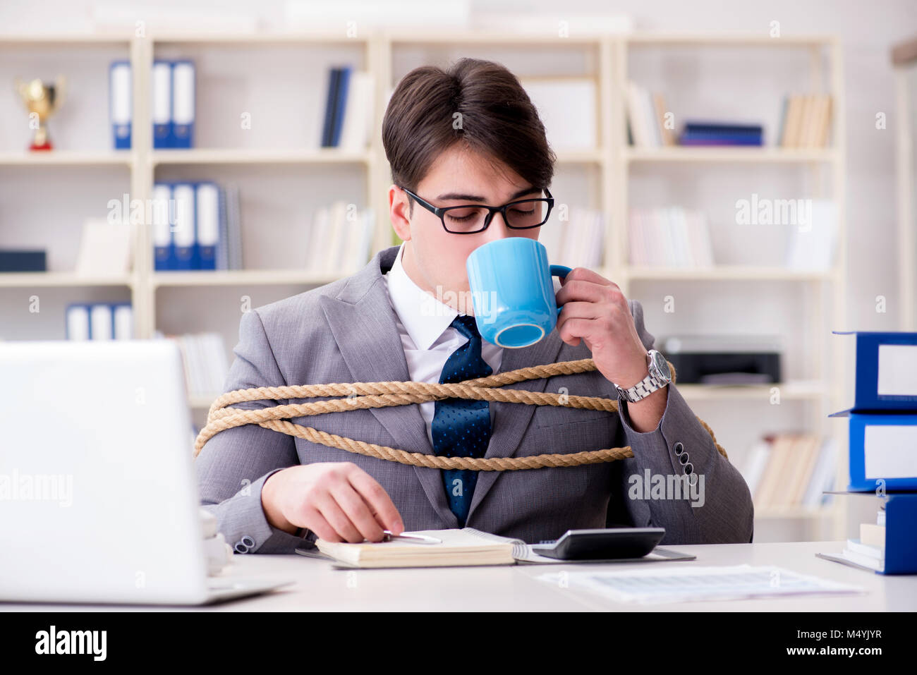 Businessman tied up with rope in office Stock Photo - Alamy