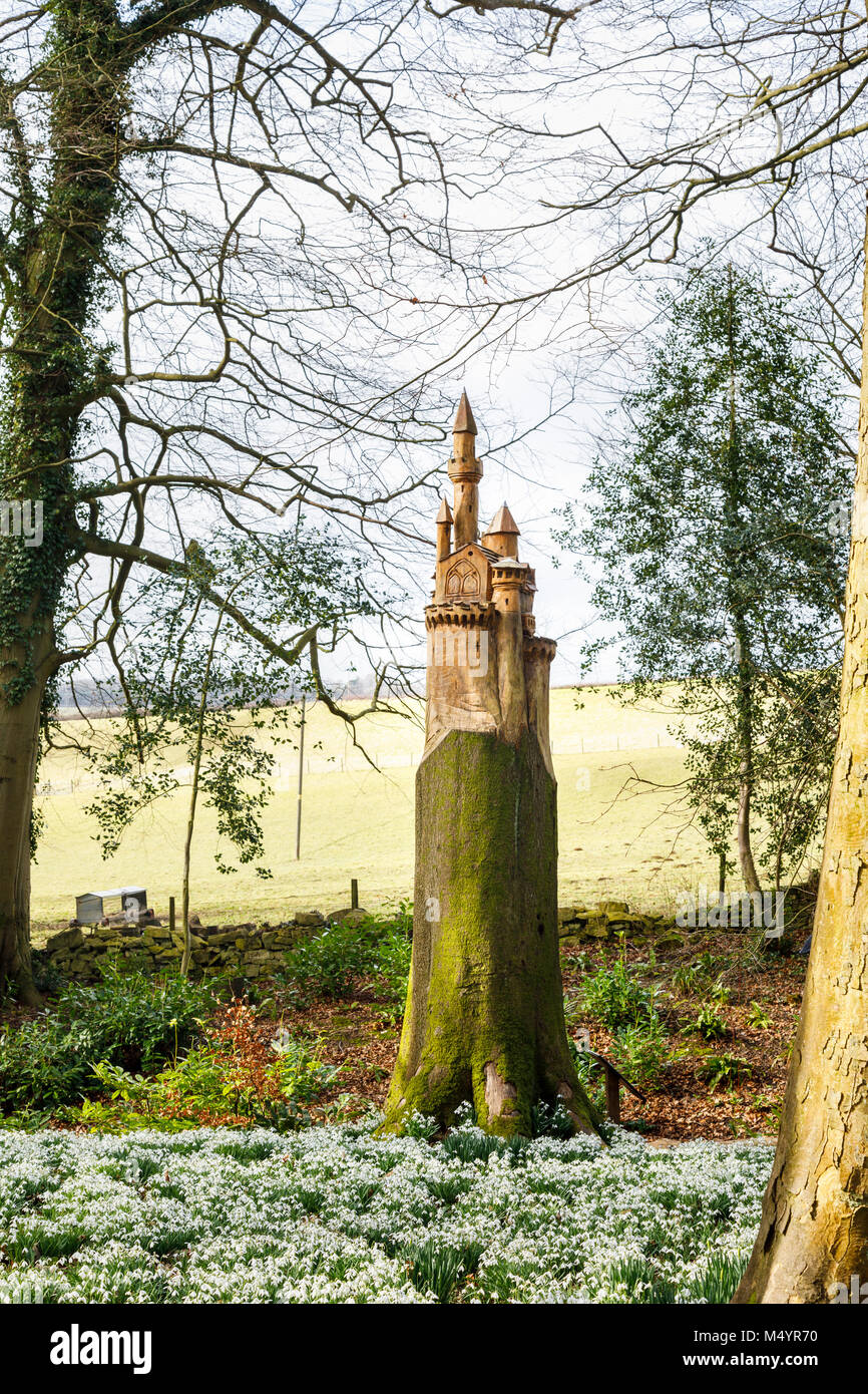 Carpet of snowdrops and nesting box carving of a castle on the stump of ...