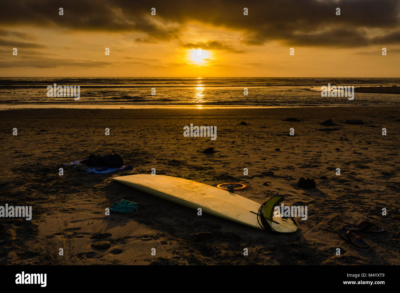 Golden glow of sun setting on beach shines light on yellow surfboard ...