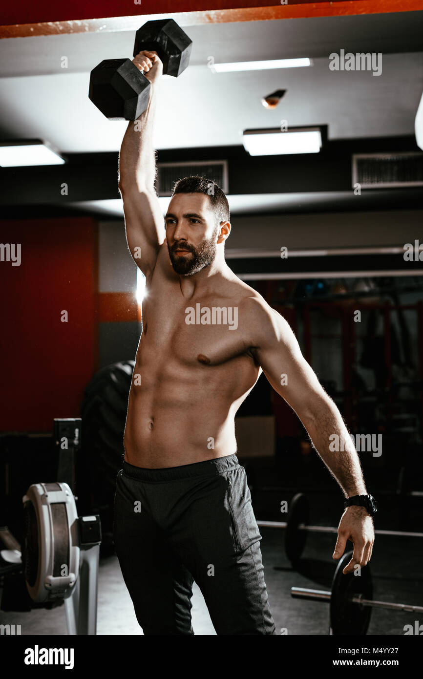 Young muscular man doing hard exercise with dumbbell on cross training ...