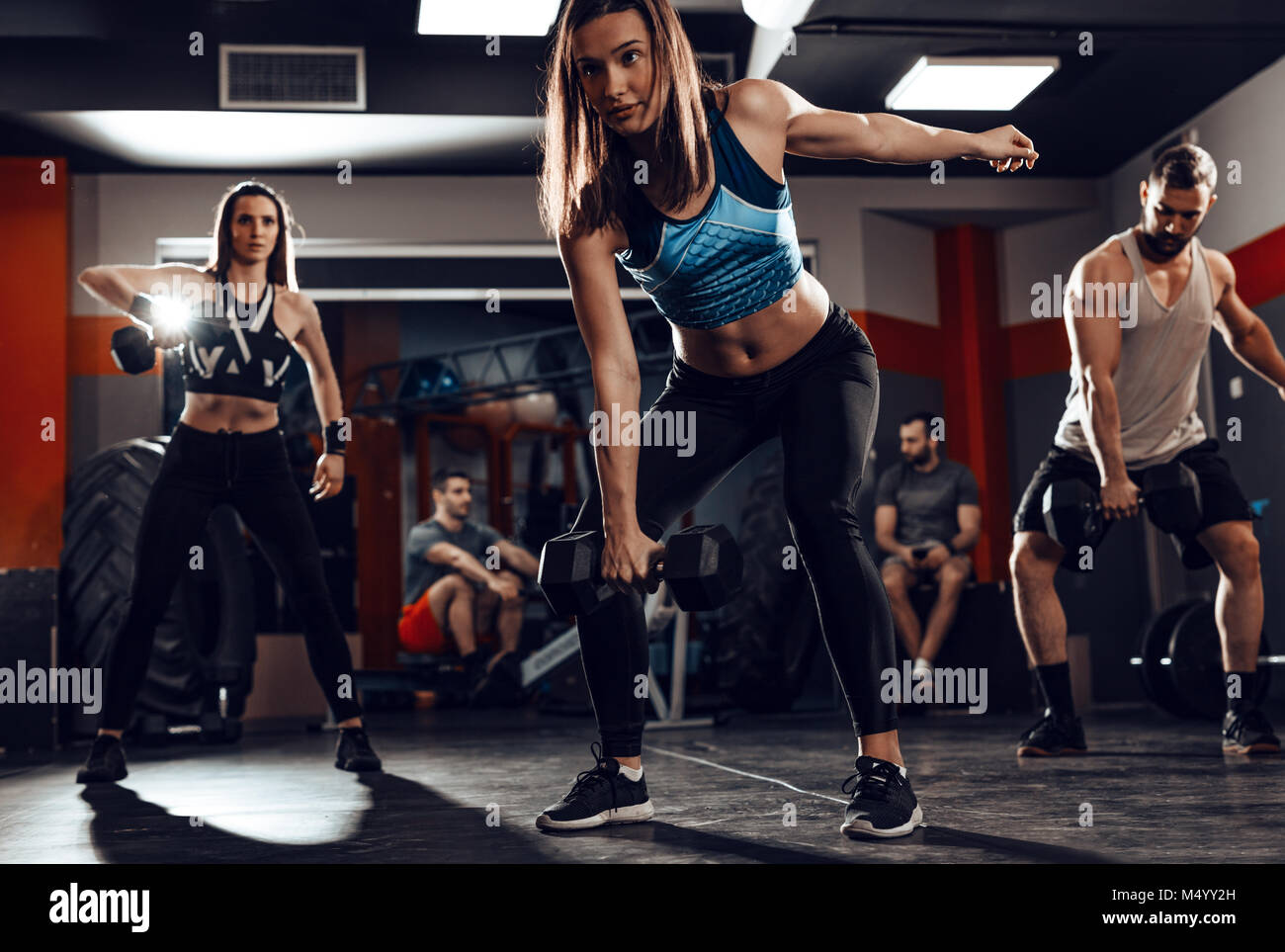 Several young friends doing hard exercise with dumbbell at the gym ...