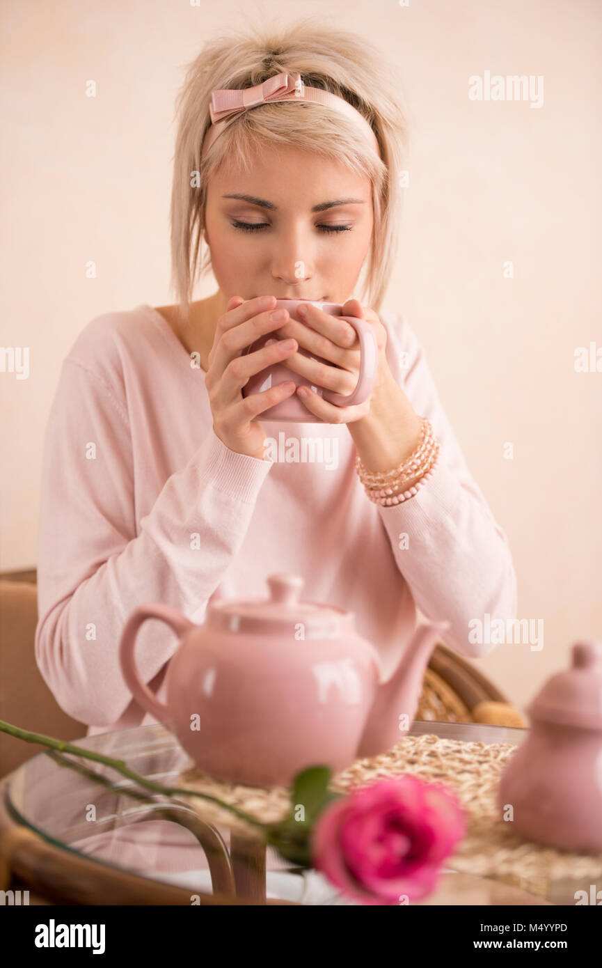 Young beautiful woman having tea-party in pink feminine style. She is ...