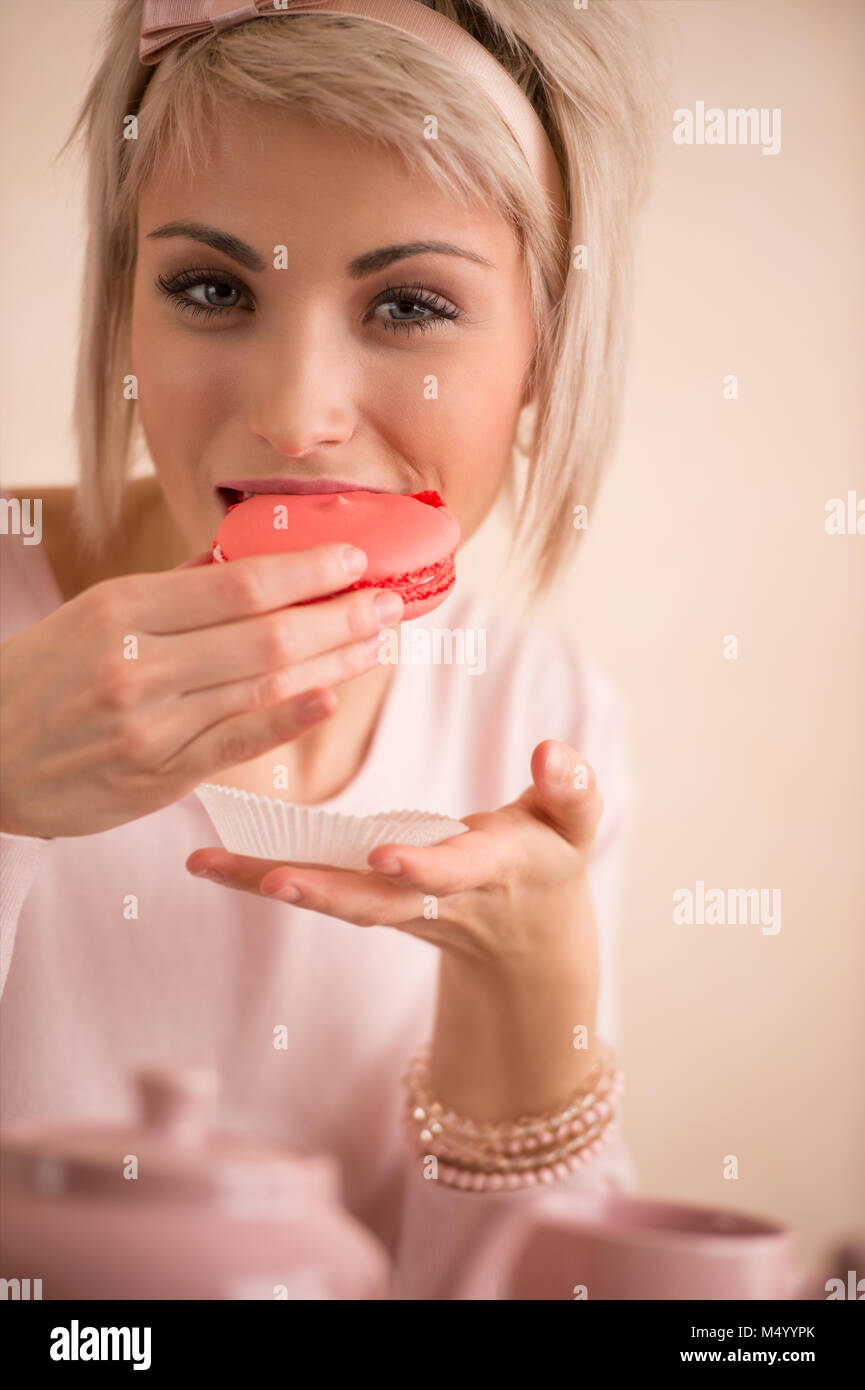 Young beautiful blond woman eating macaroon while having tea-party. She ...