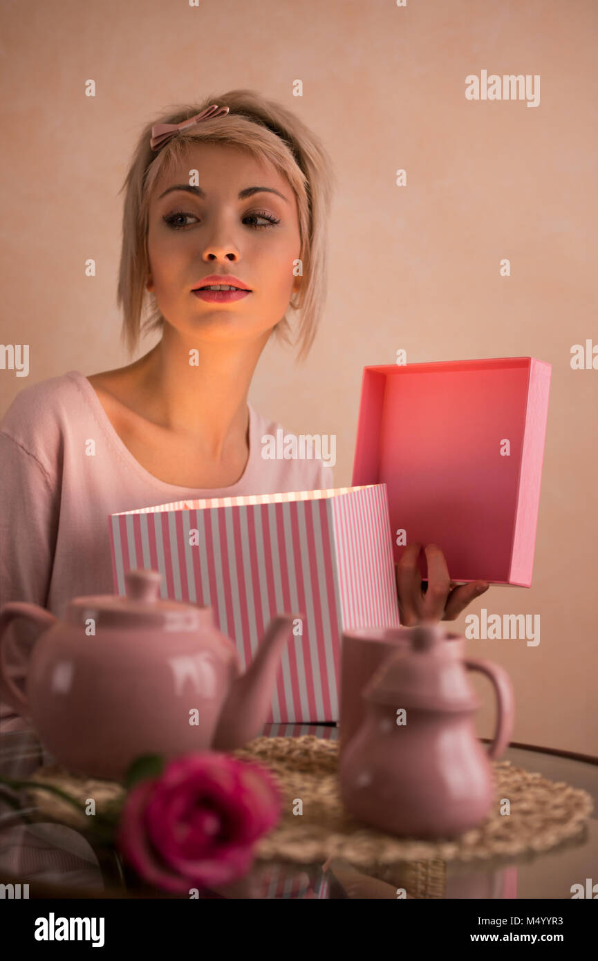 Young beautiful woman opening gift box while having tea-party. She is ...