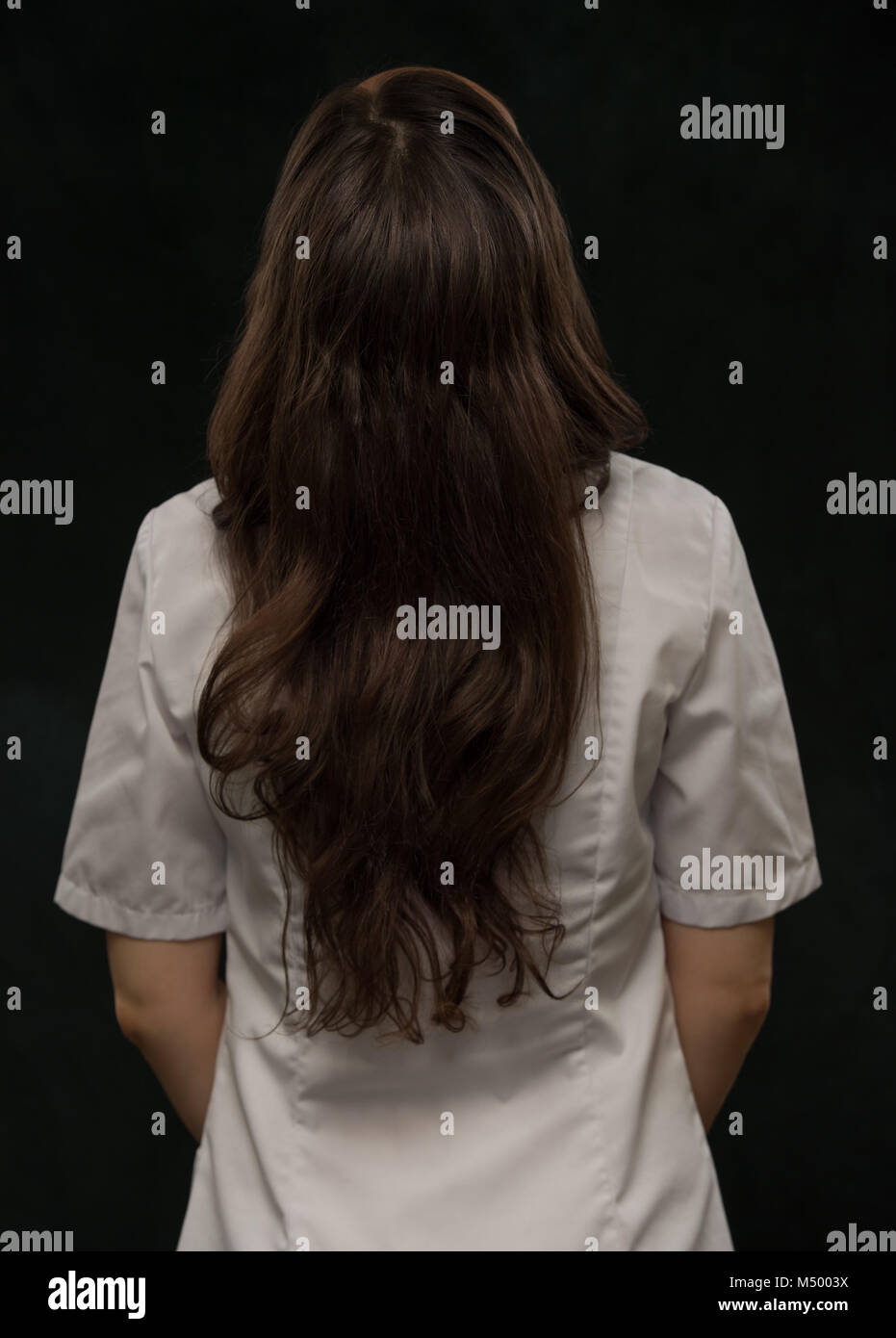 Female doctor standing in front of black background. Photo from behind ...