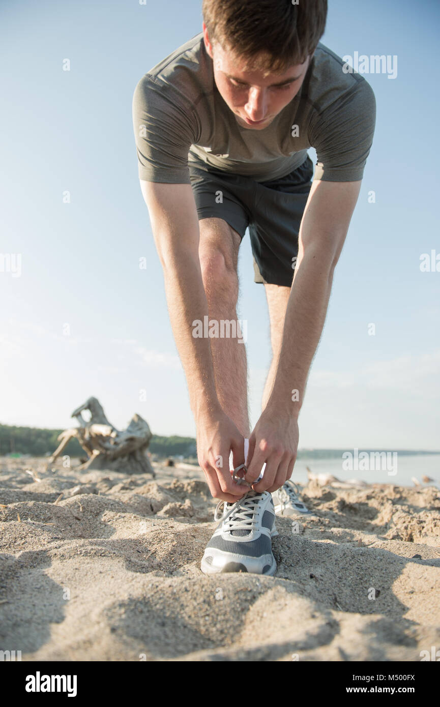 Young man is tying his shoe while running at sunny beach Stock Photo ...