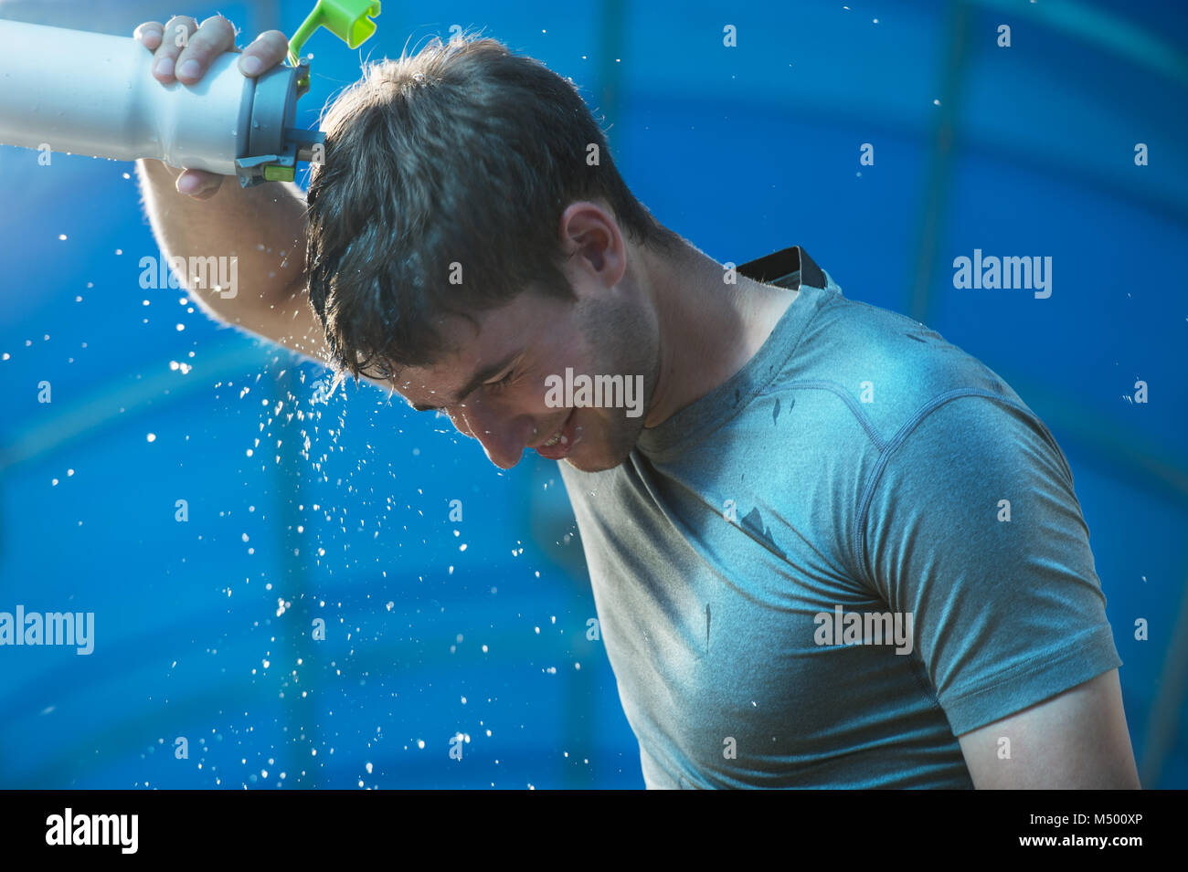 Young tired athlete splashing and pouring fresh water on his head to ...