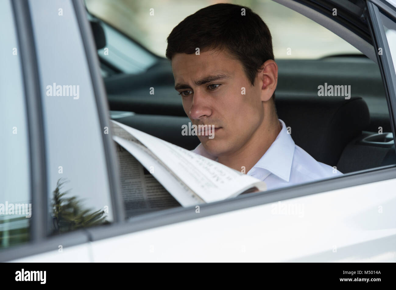 Young businessman reading newspaper on back seat of his car Stock Photo ...