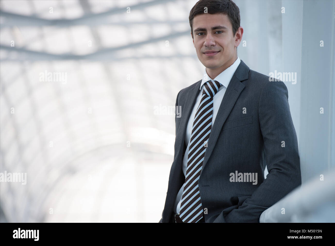 Portrait of handsome confident young businessman standing relaxed, smiling happy, looking at ...