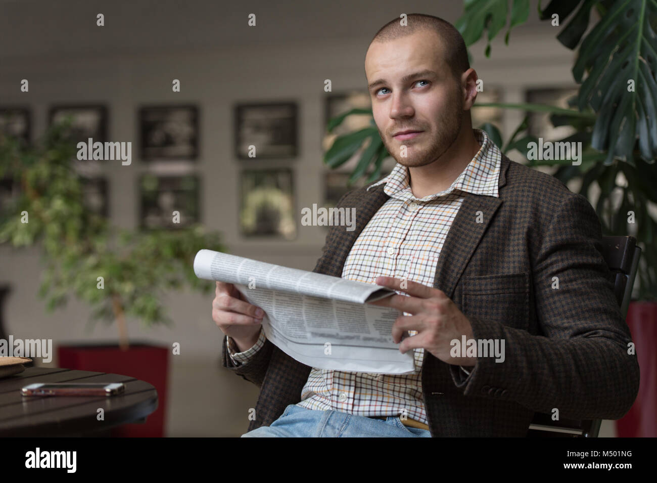 Businessman reading newspaper on chair at office building hall or cafe ...
