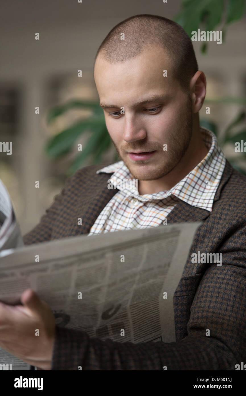 Businessman reading newspaper on chair at office building hall or cafe ...