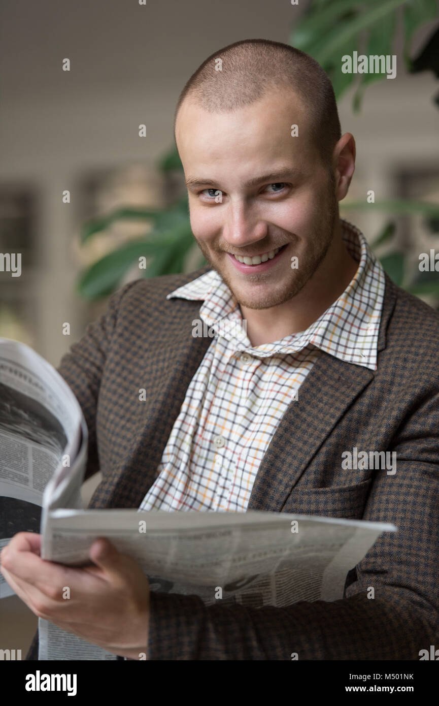 Businessman reading newspaper on chair at office building hall or cafe ...