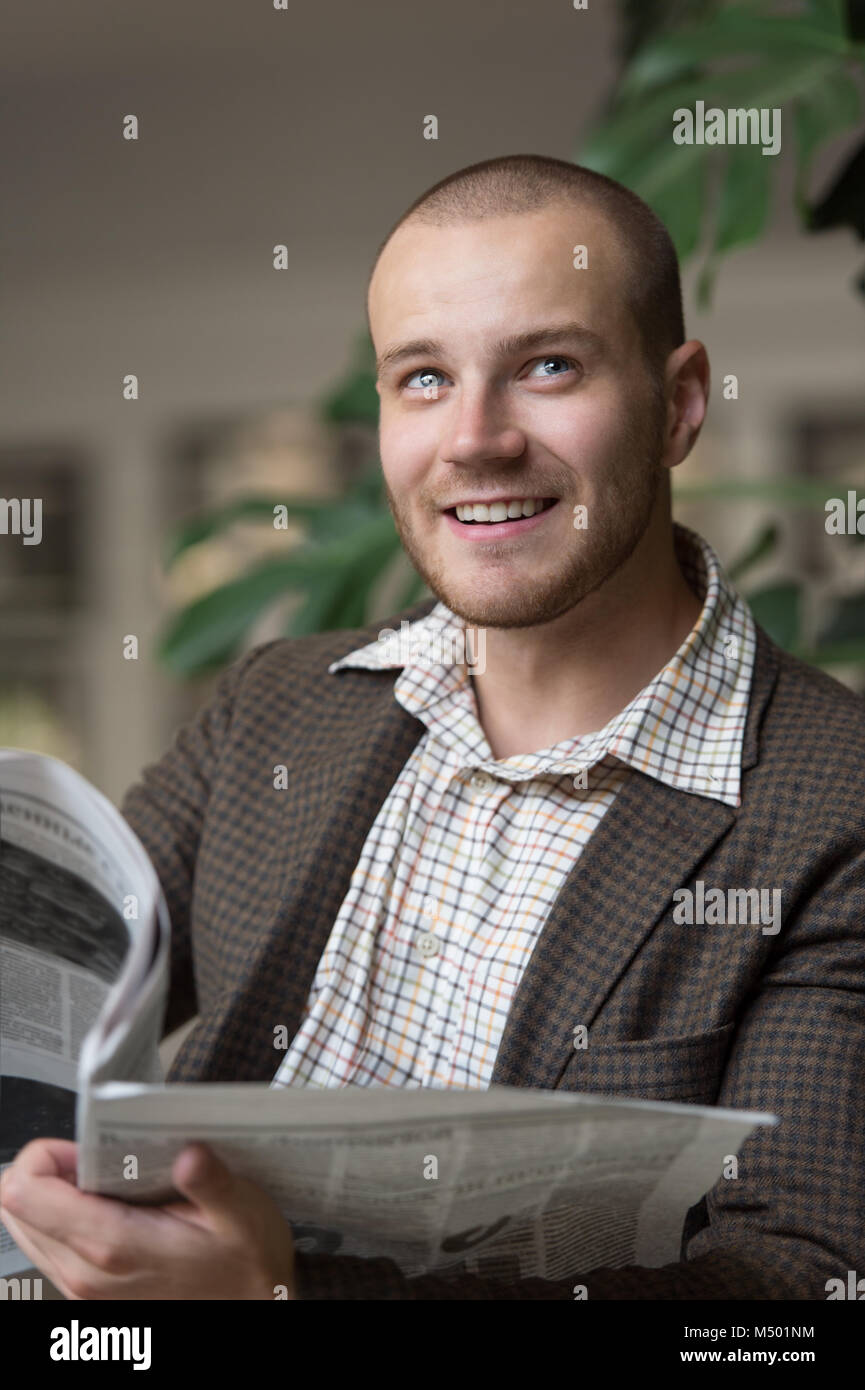 Businessman reading newspaper on chair at office building hall or cafe ...