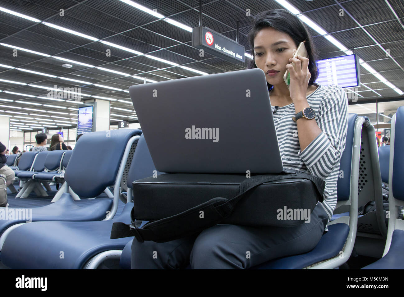 A young woman is working on a computer in an airport lobby while ...