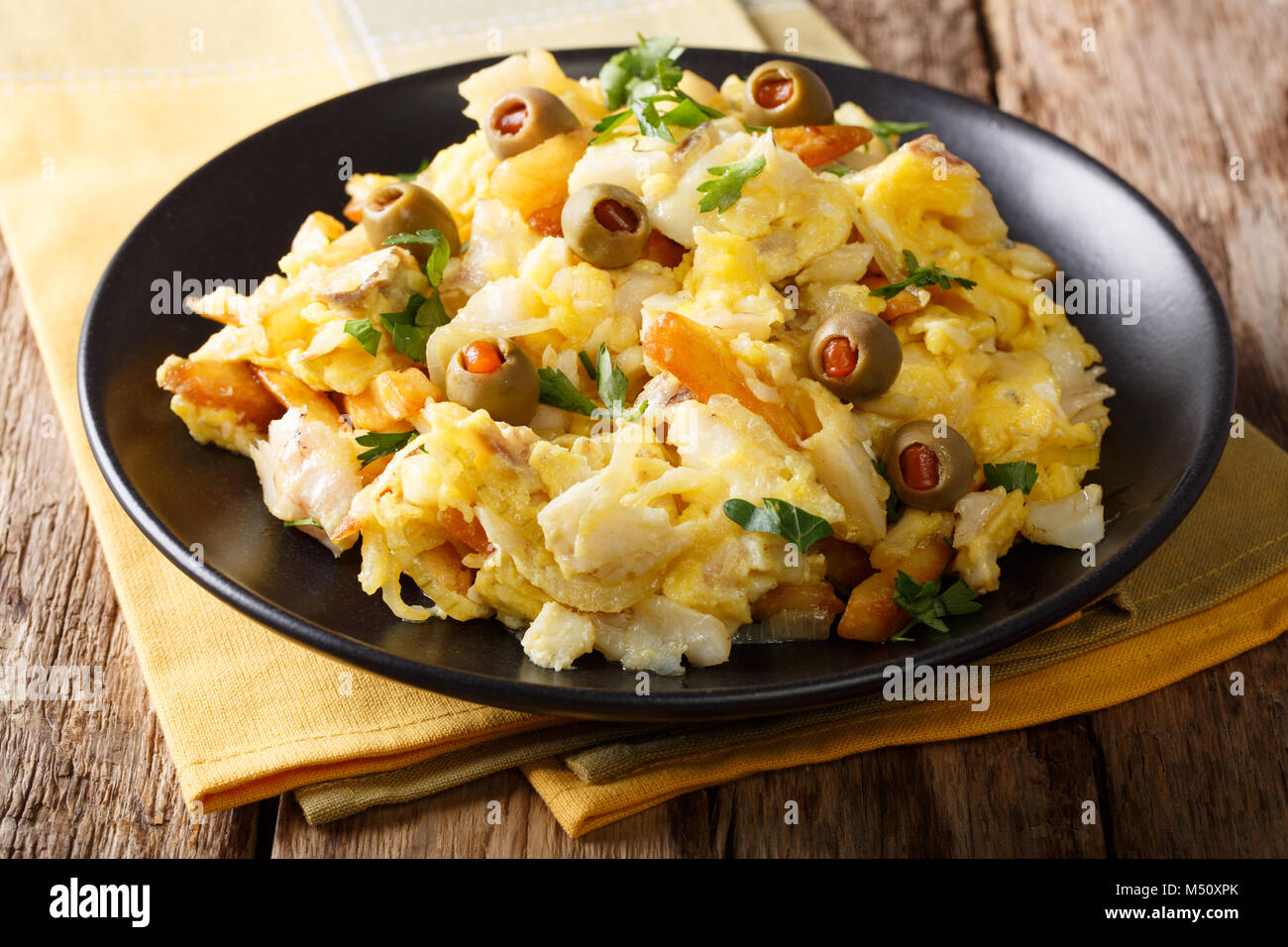 Fried shredded cod with potatoes, onions, egg and olive on a plate on ...