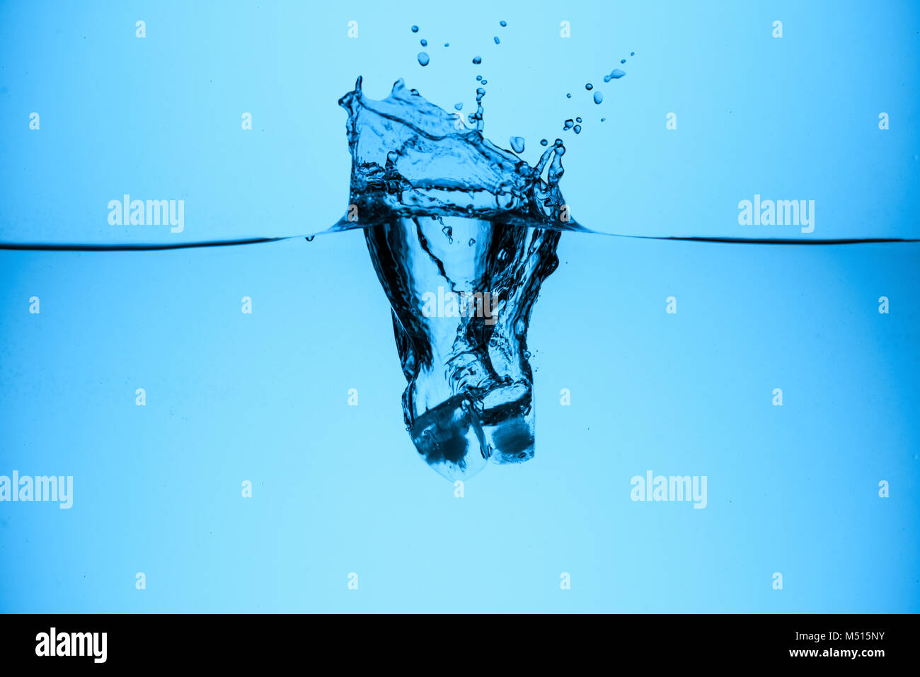 ice cube splashing in water, isolated on blue Stock Photo - Alamy