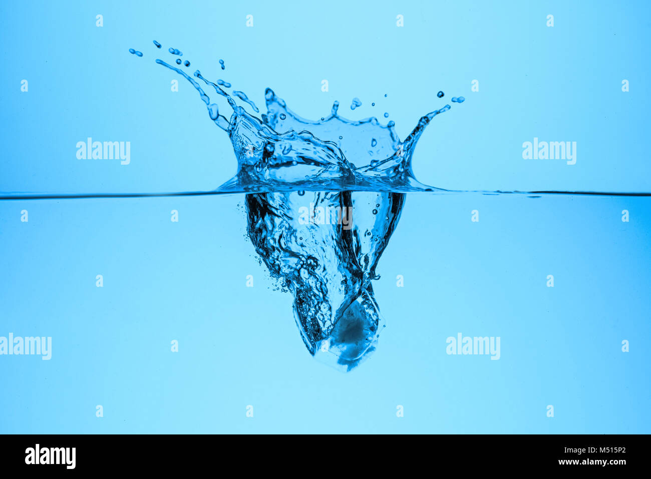 ice cube in clear water with splash, isolated on blue Stock Photo - Alamy